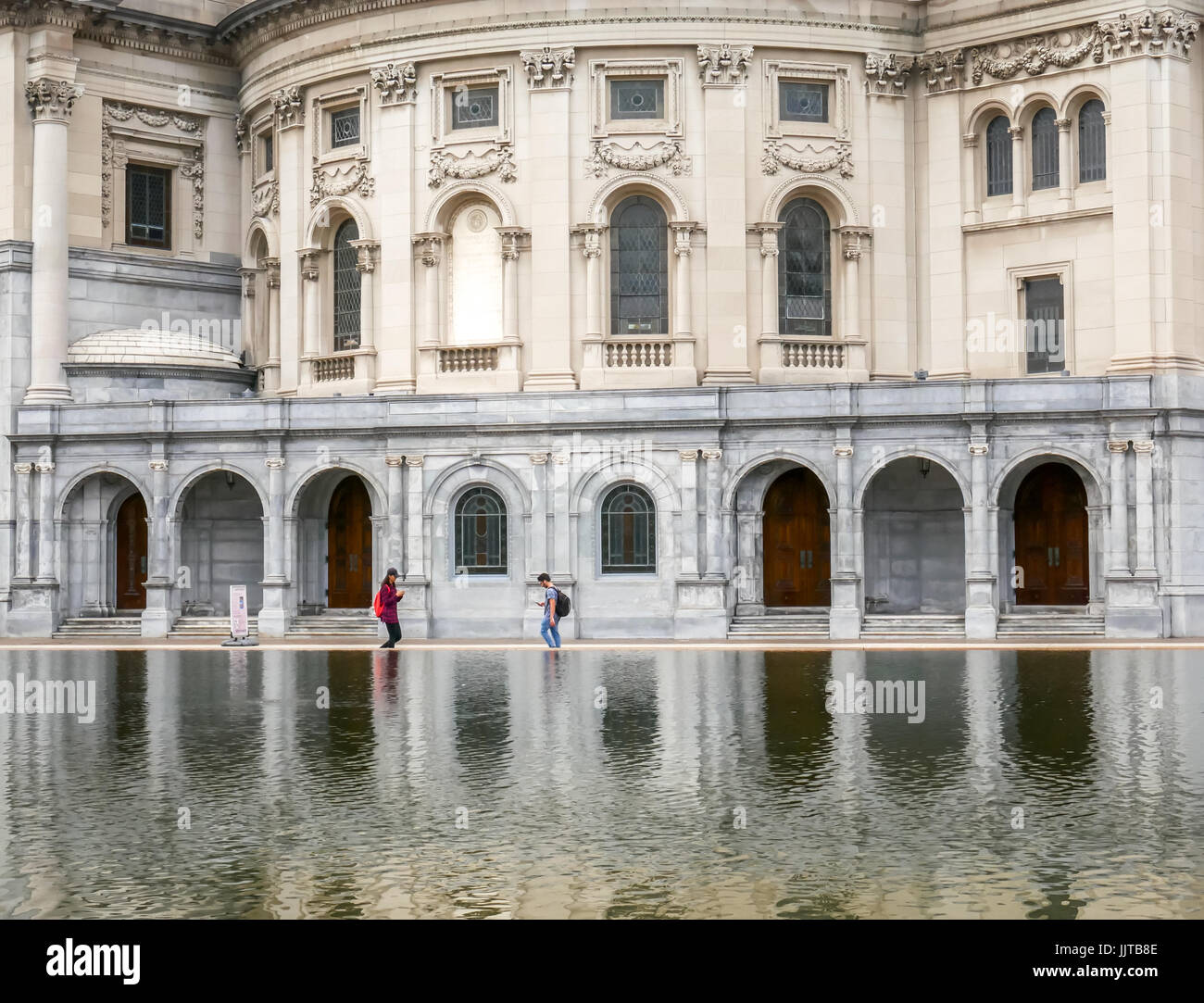 Two young people looking at their phones while walking past the ...