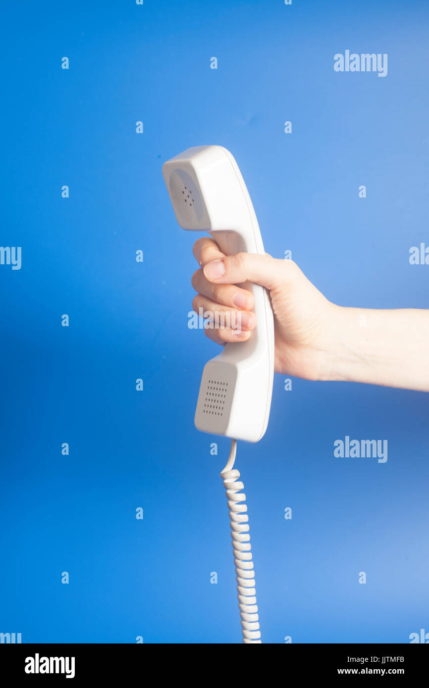 Hand holding white telephone tube on blue background Stock Photo - Alamy