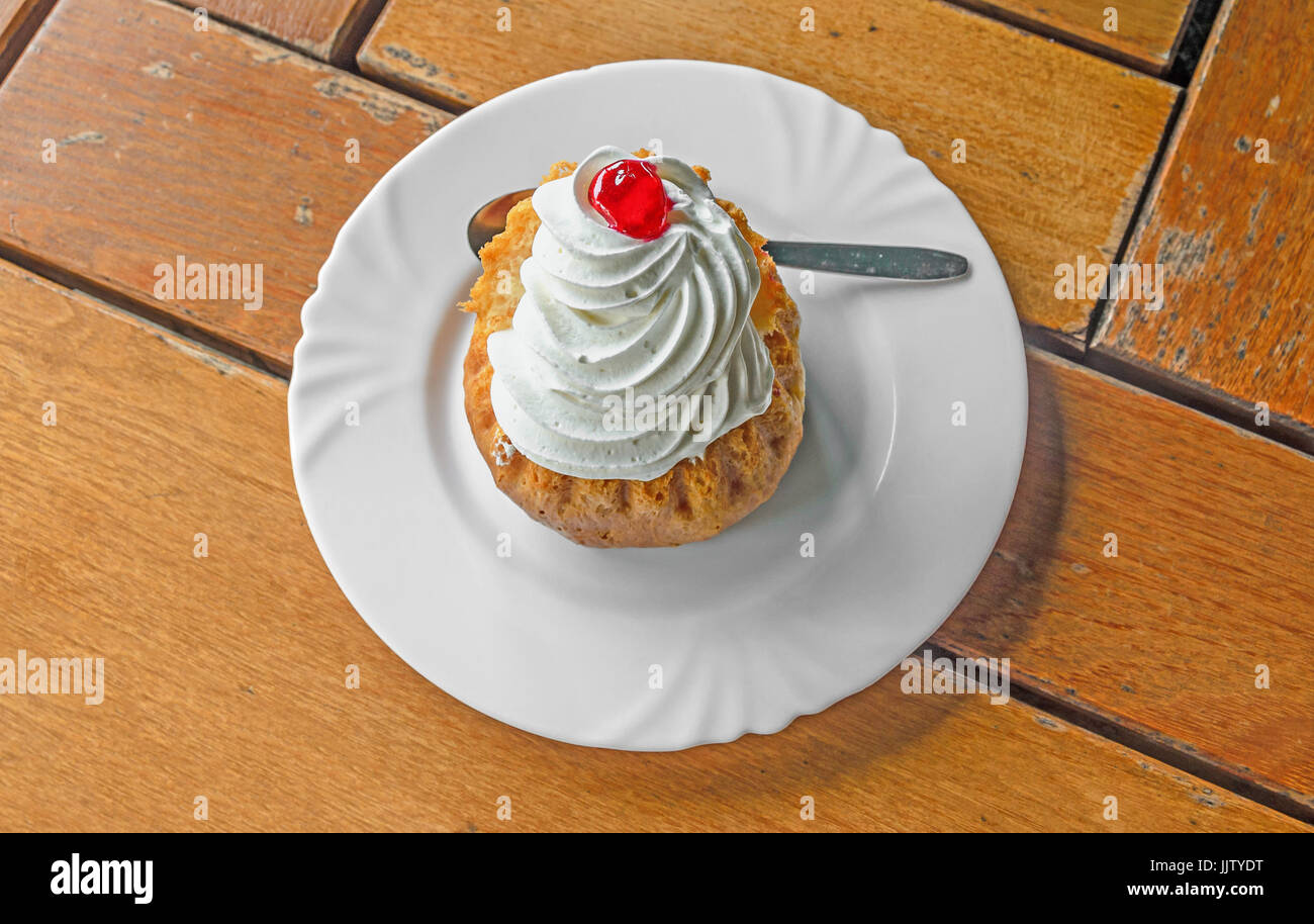Savarin cake with cream and syrup, silver spoon, white plate on wood ...