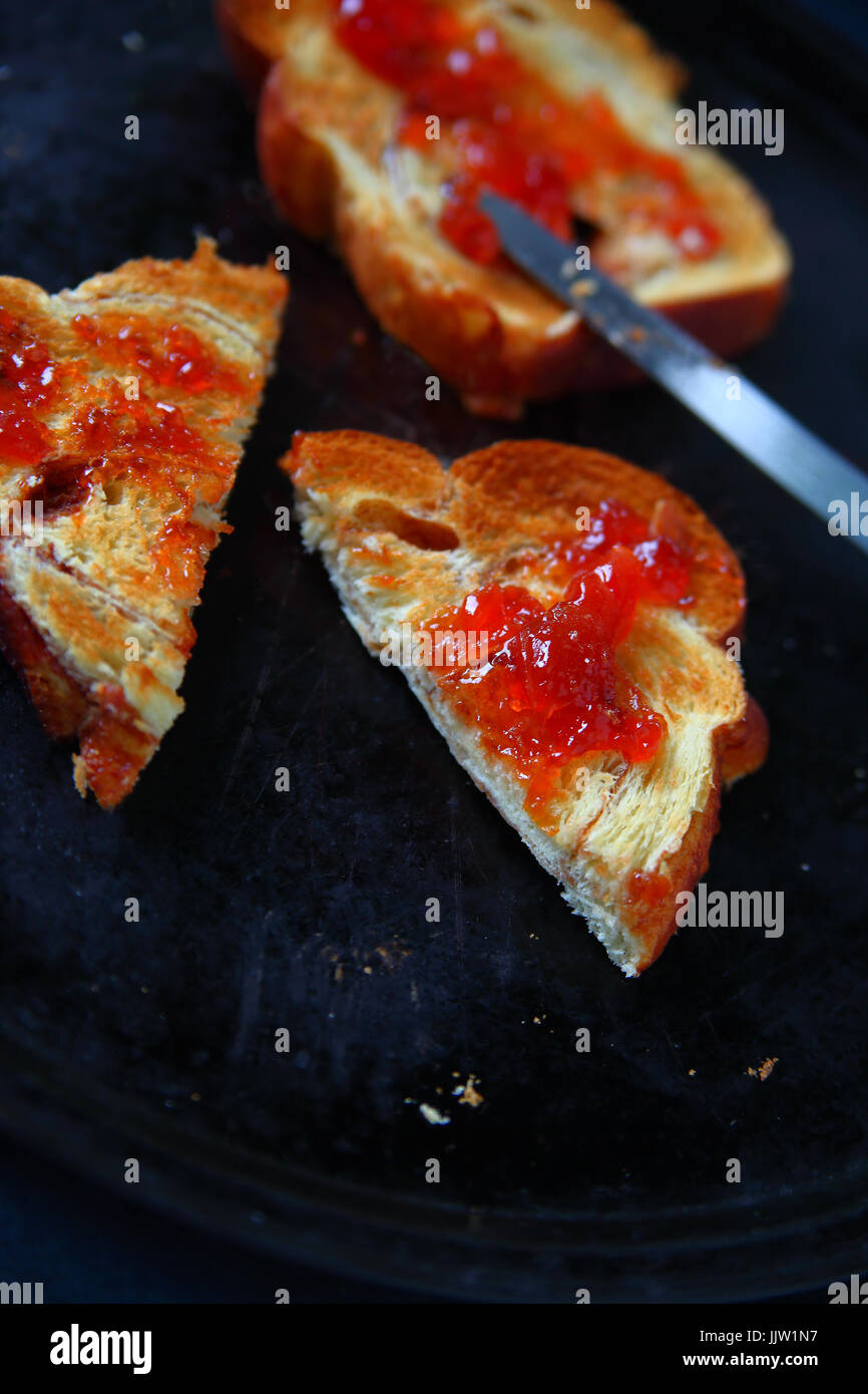 Slices of toast with raspberry jam, one cut in half, on a dark metal ...