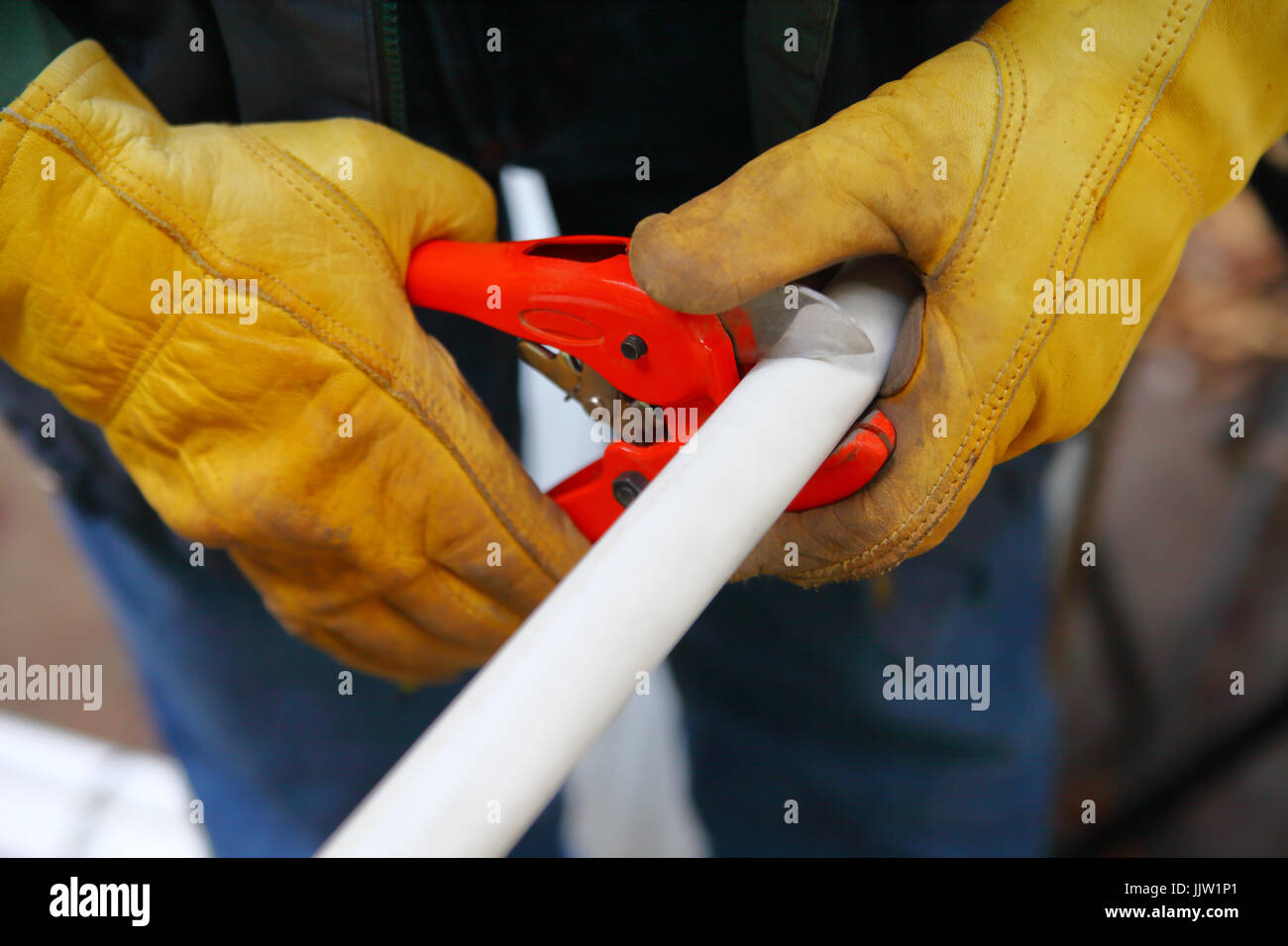 Handyman with work gloves makes a cut in a piece of plastic piping ...