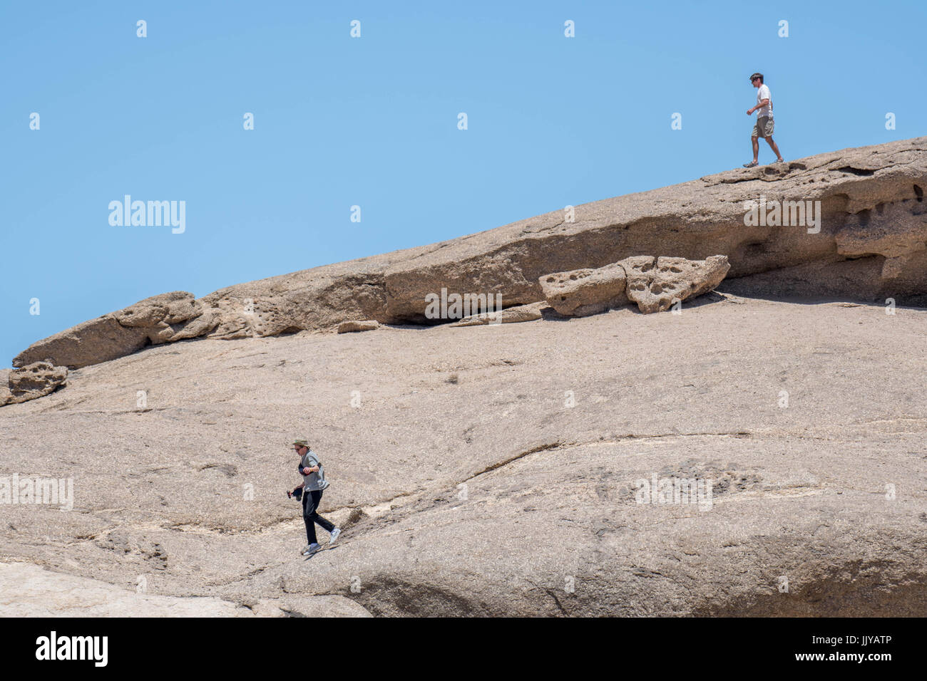 Tourists walking down large rock formations in the Namib desert, in ...