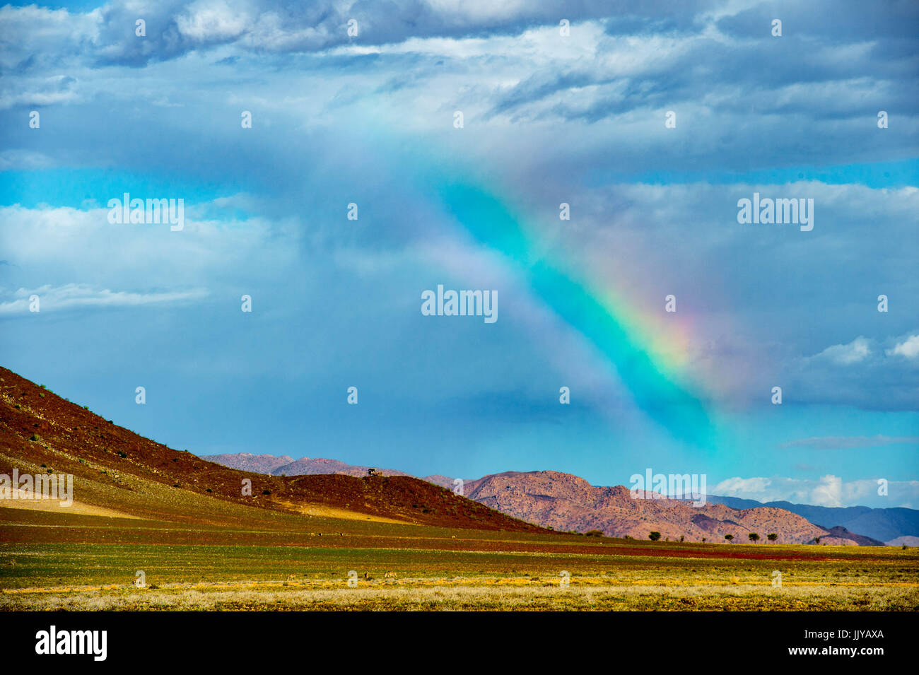 A rainbow arches over mountain landscape in the Namib desert, located ...