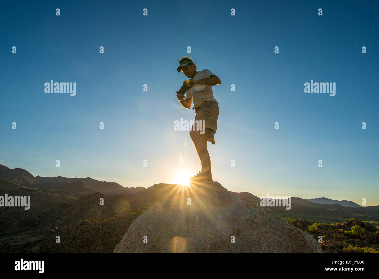 A man stands on top of a large boulder while photographing on a cell ...