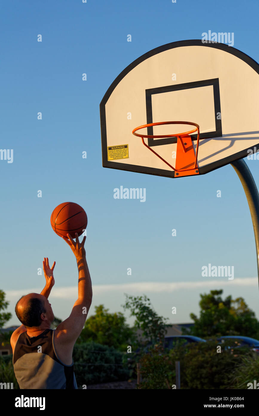 Man of mixed race throwing a basketbal through the hoop at sunset in an ...