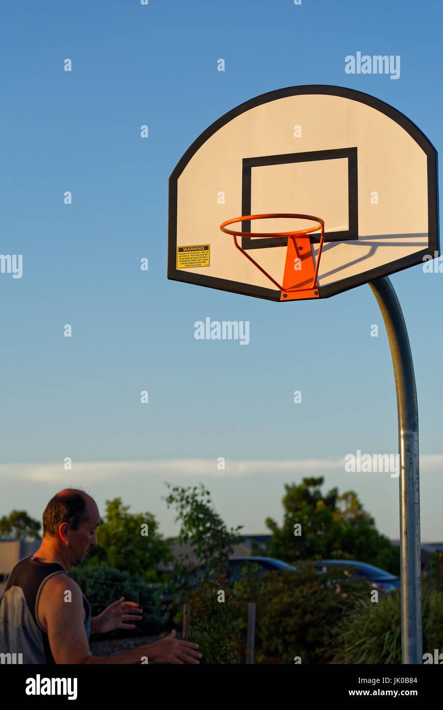 Man of mixed race throwing a basketbal through the hoop at sunset in an ...