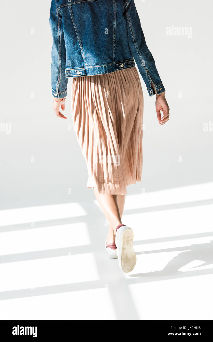 Rear view, low angle shot of woman in beige skirt and denim jacket ...