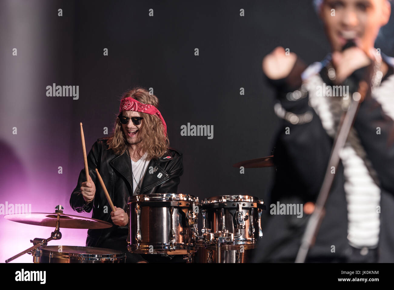 Smiling young man playing drums set with singer on stage Stock Photo ...