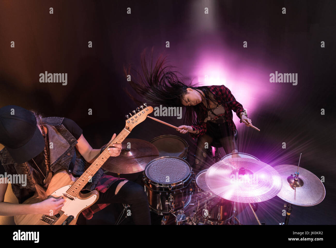 Excited young women with drums set and electric guitar performing rock ...