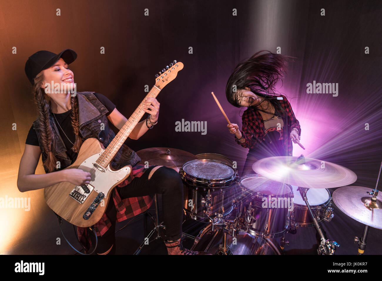 Excited young women with drums set and electric guitar performing rock ...