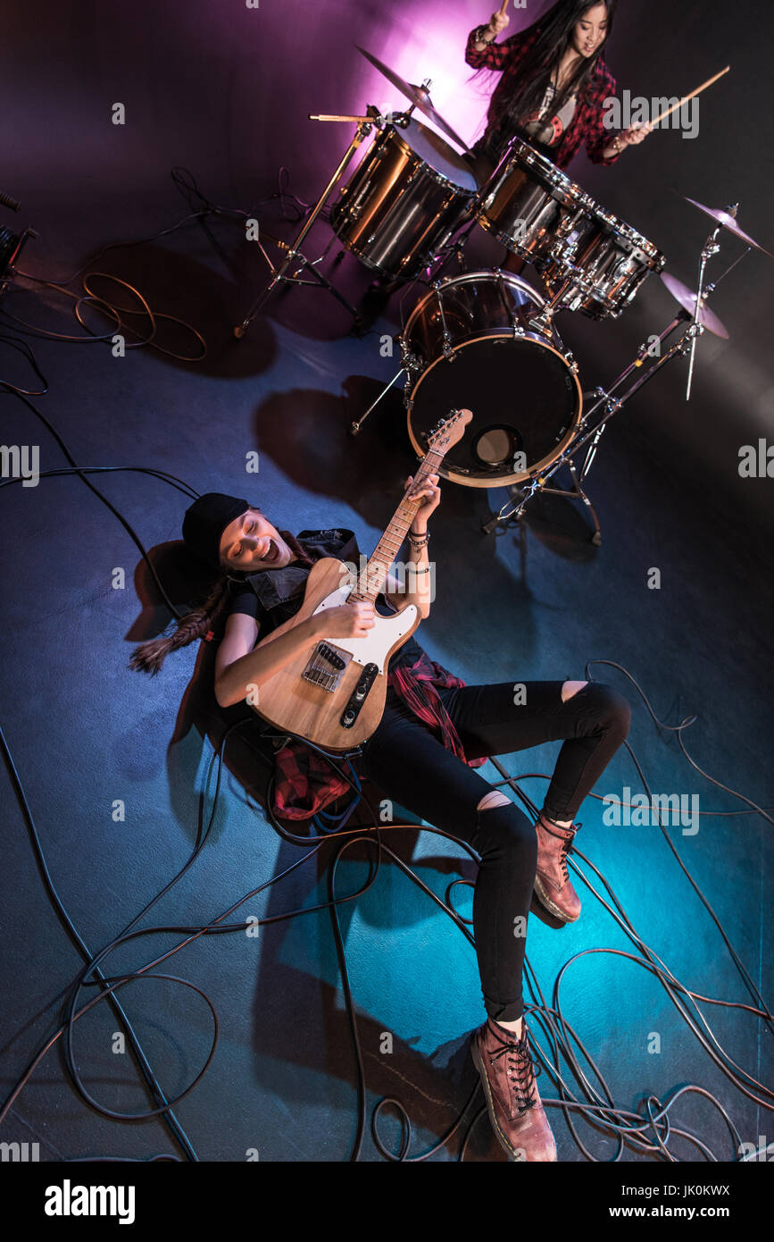 Excited rock and roll girl lying on stage and playing hard rock music ...
