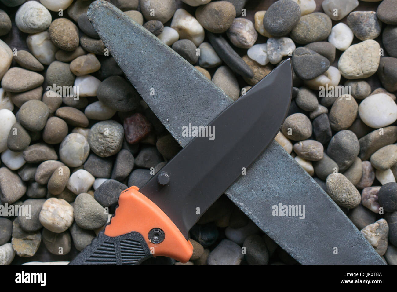 survival folding knife with sharpener stone on small rocks. closeup ...