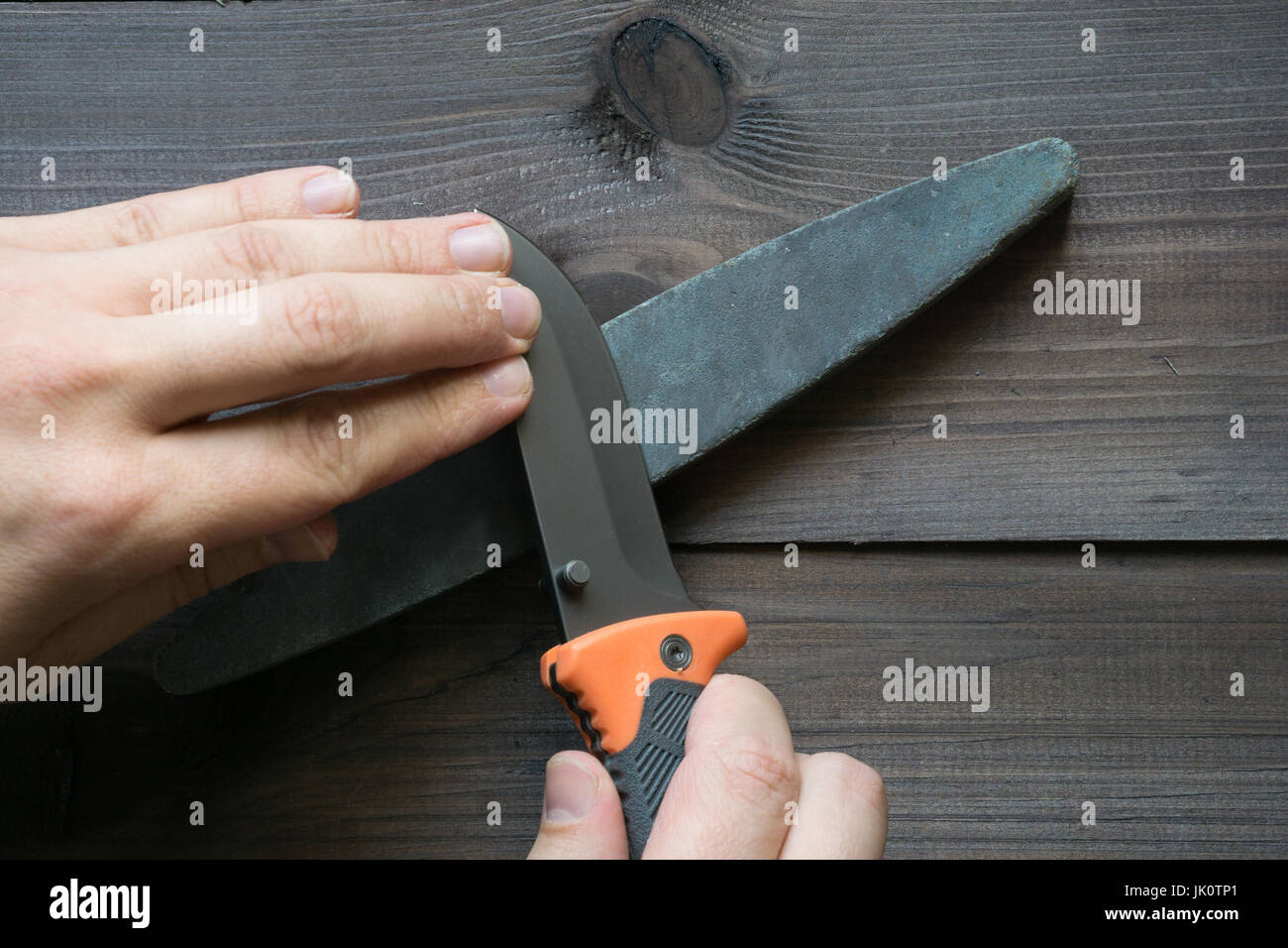 man sharpening survival knife on a sharpener stone. top view on dark ...