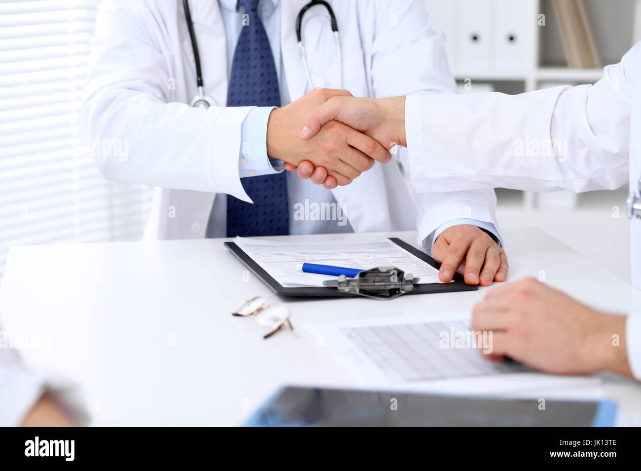 Two doctors shaking hands to each other sitting at the table in ...