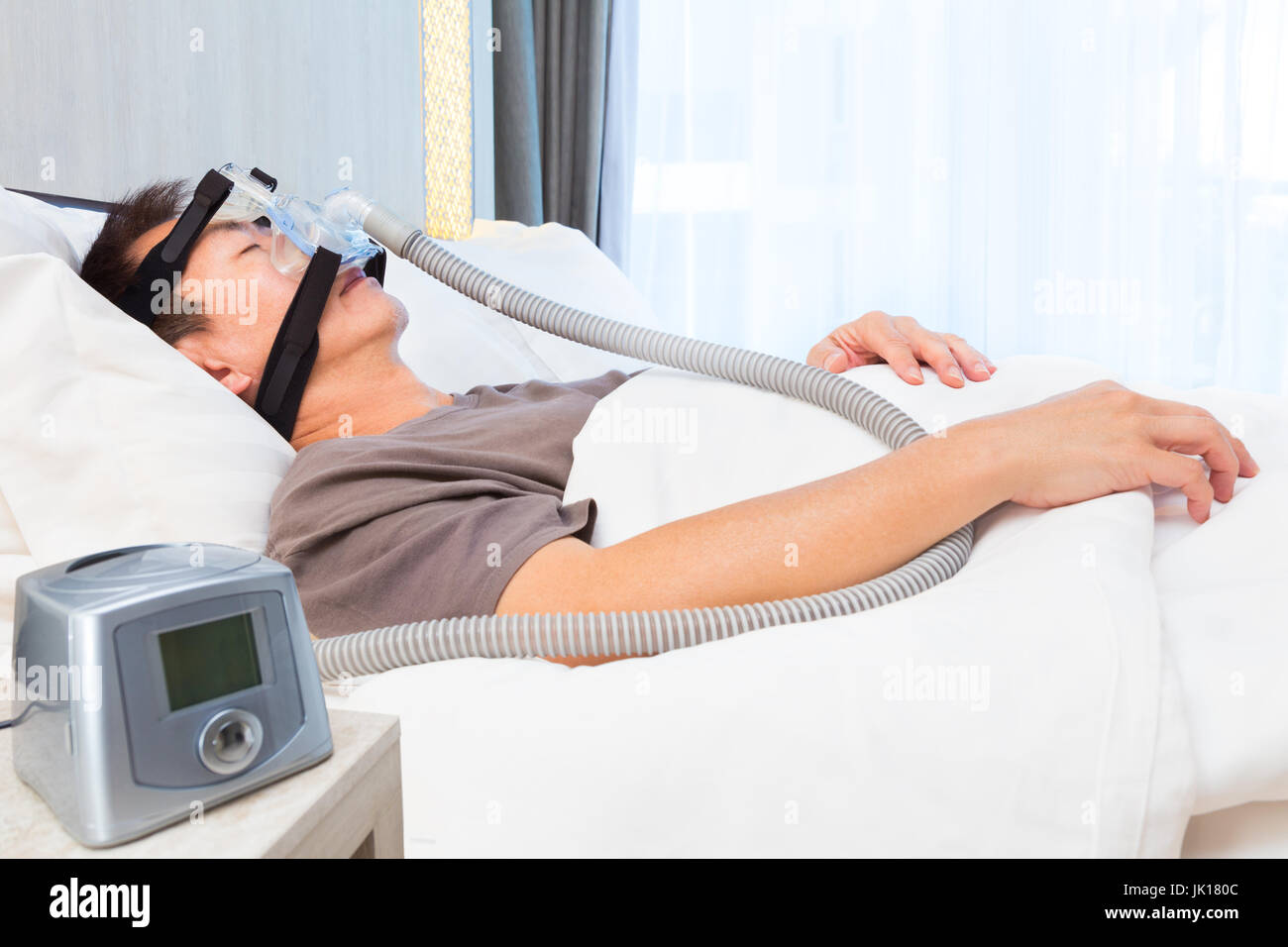 middle age asian man sleeping in his bed wearing CPAP mask connecting ...