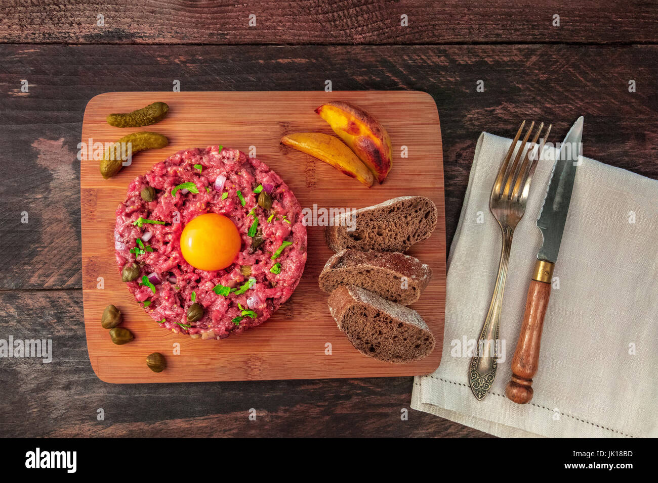 A photo of a steak tartare with a raw egg yolk, gherkins, capers, rye ...