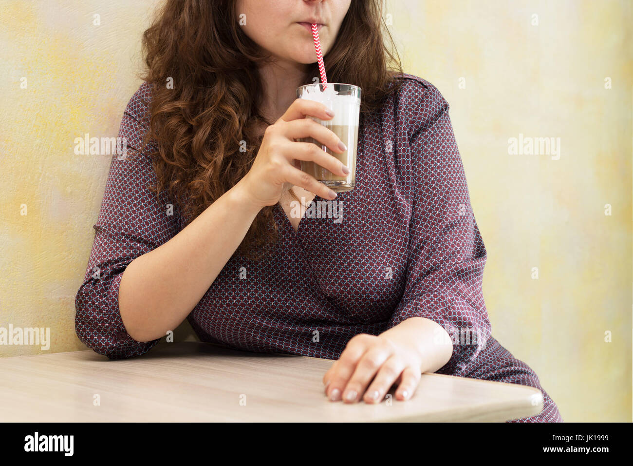 young woman sitting in cafe and drinking coffee cold cocktail through a ...