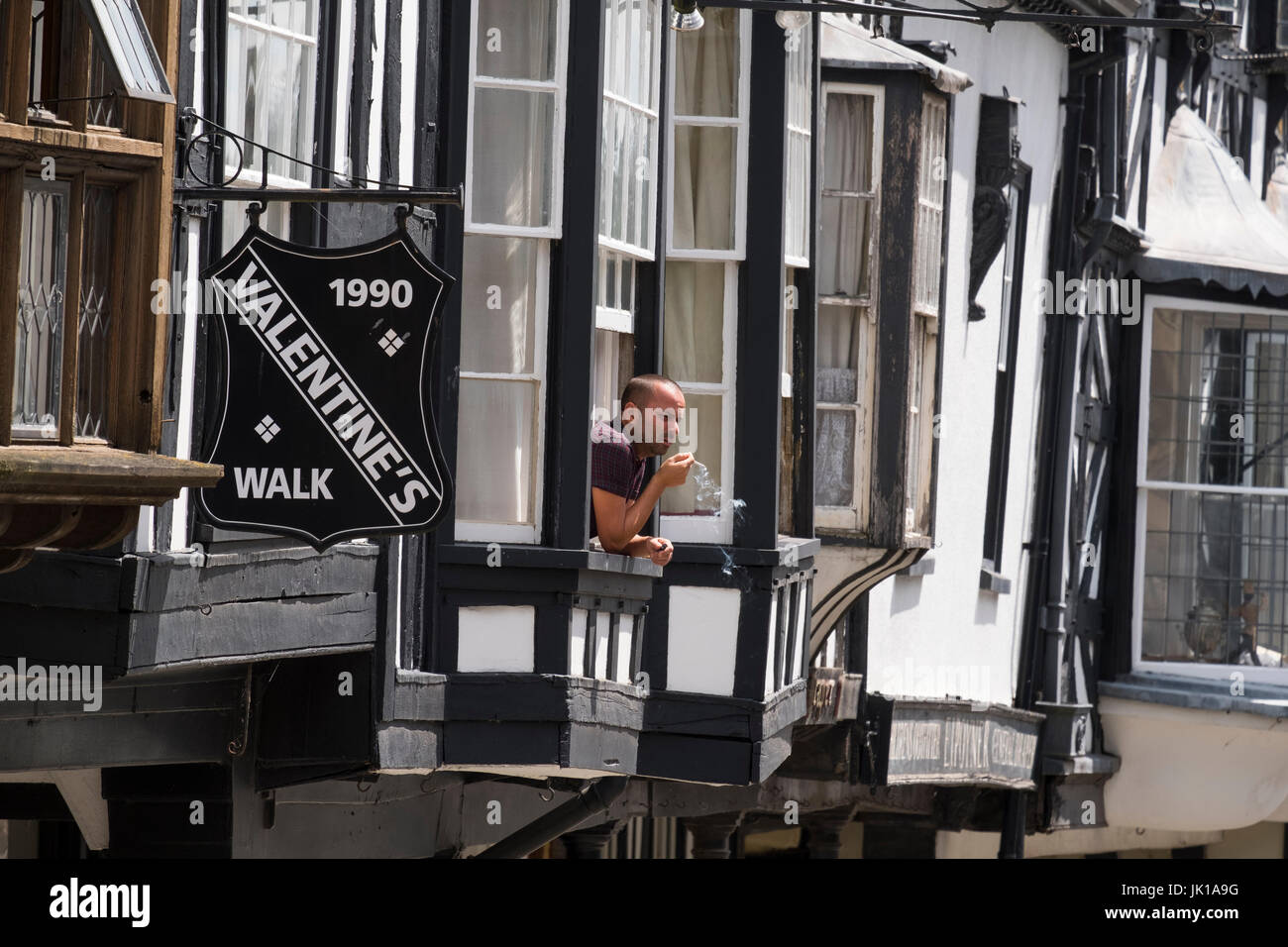 A man smoking while leaning out of a window in a row of half timbered ...
