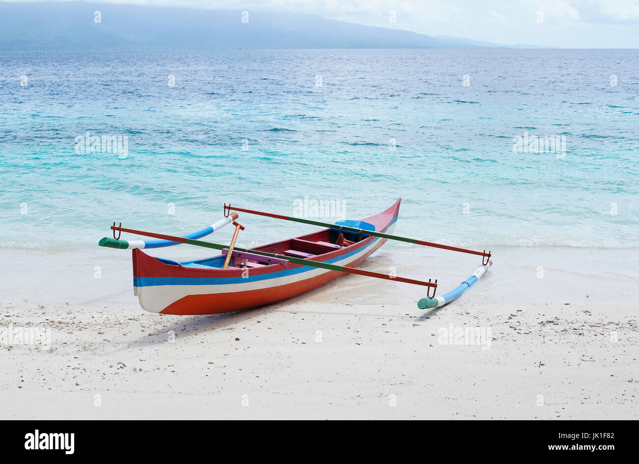 Red white blue colored small empty canoe boat stranded on a tropical ...