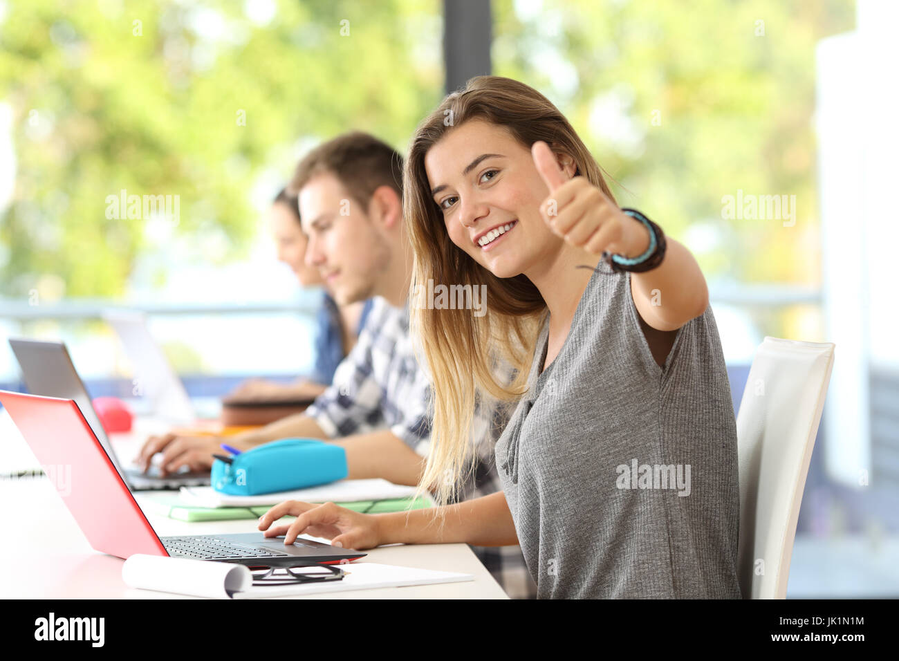 Happy student looking at you with thumbs up in a classroom with ...