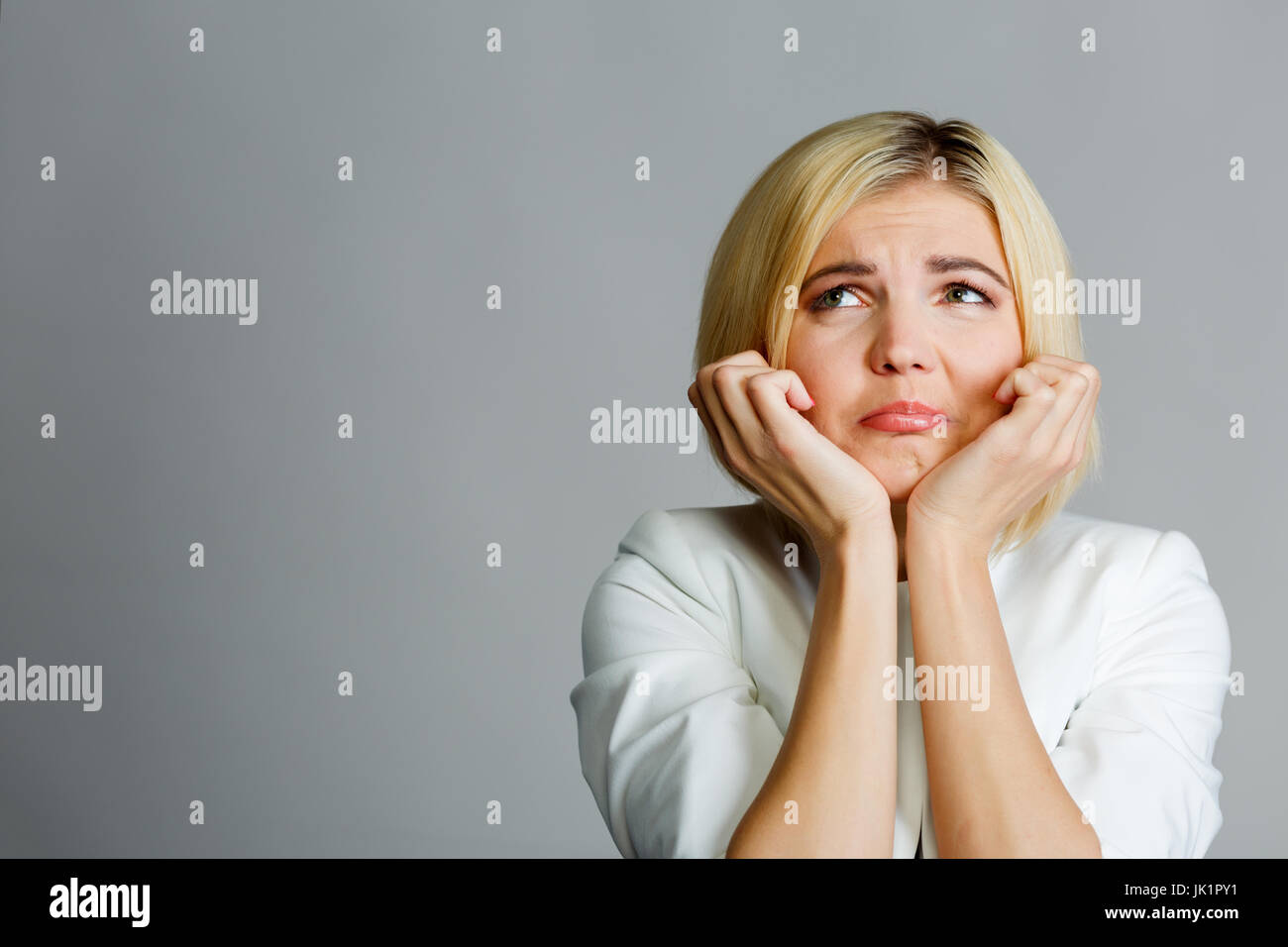 Sad woman with hand at chin on empty gray background Stock Photo - Alamy