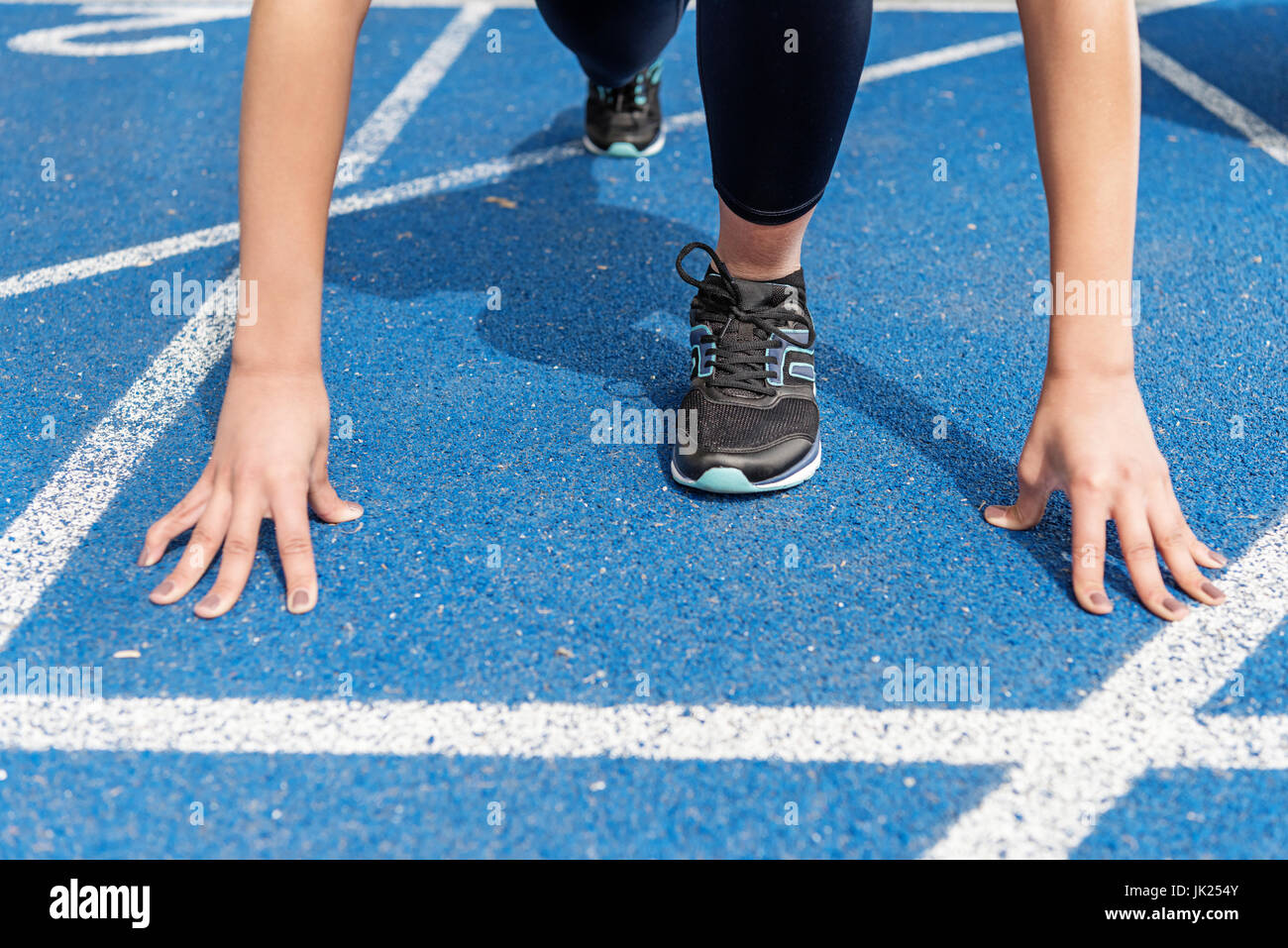 Close-up partial view of sportswoman on starting line at running track ...