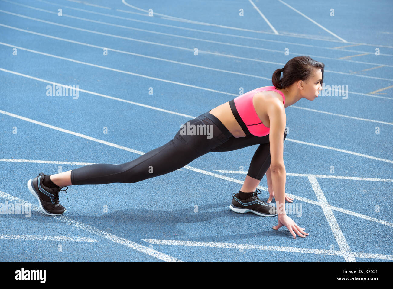 Side view of athletic young woman in sportswear on starting line ready ...