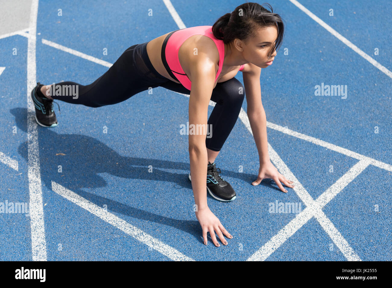Concentrated athletic young runner on starting line at running track ...