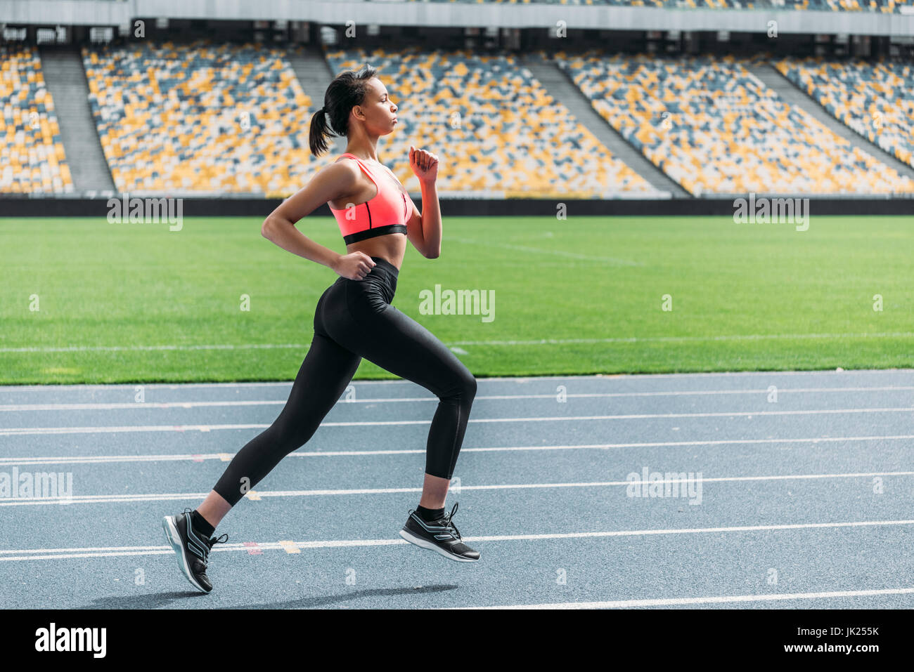 Side view of athletic young woman in sportswear sprinting on running ...