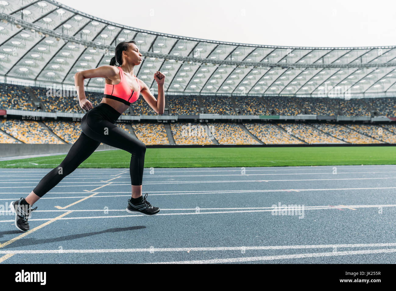 Side view of athletic young woman in sportswear sprinting on running ...