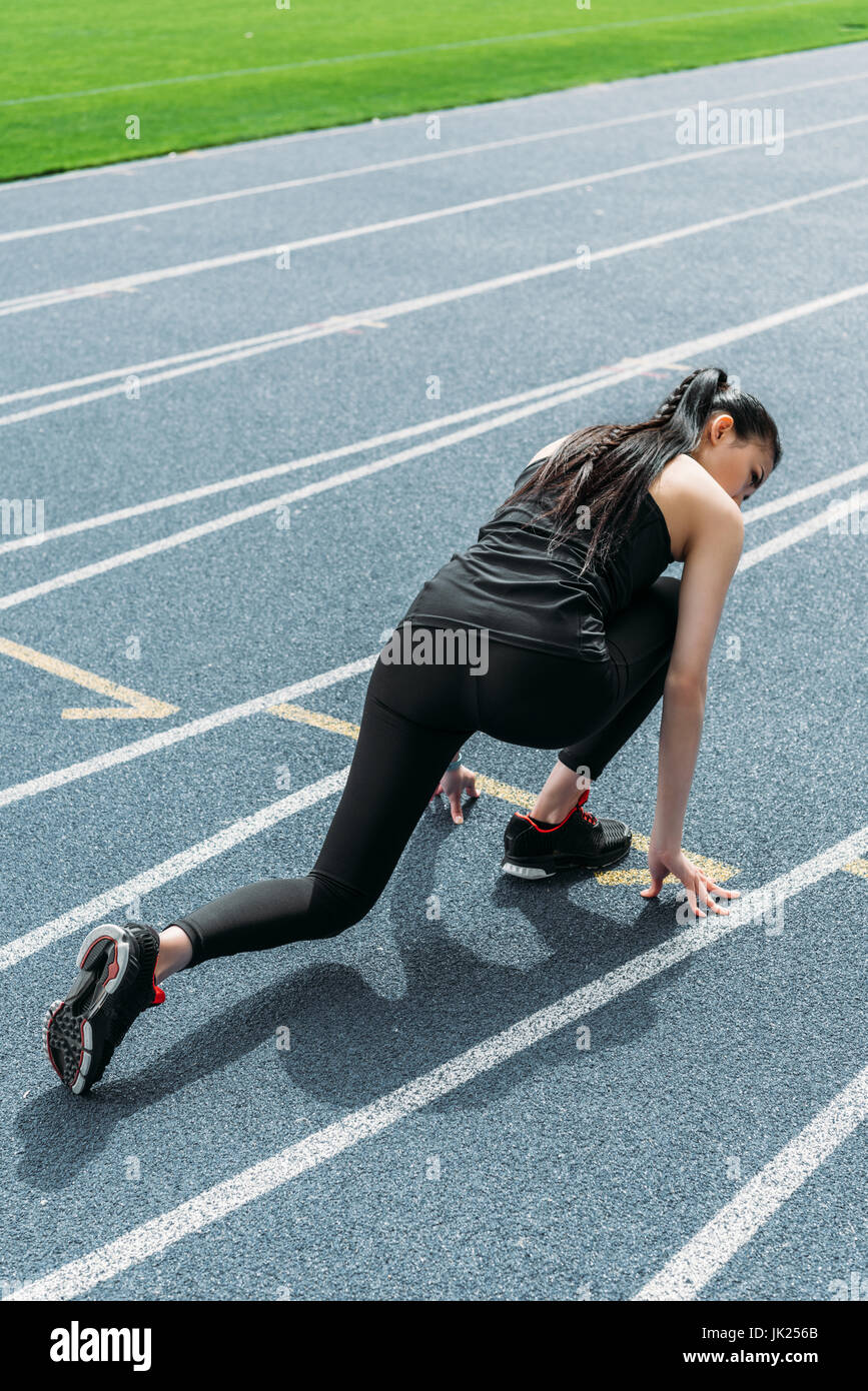 Back view of young sportswoman in starting position on running track ...