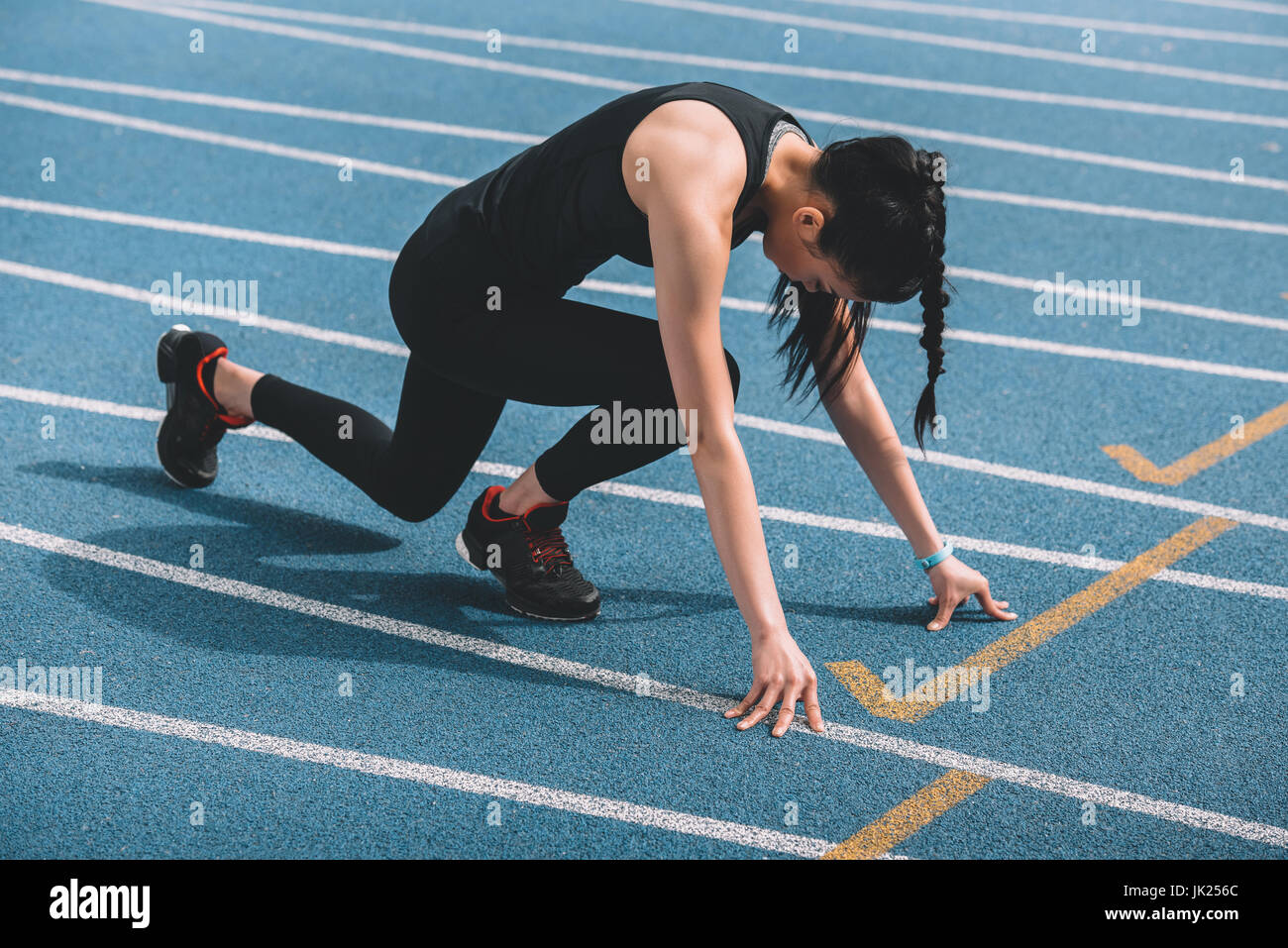 Concentrated young sportswoman in starting position on running track ...