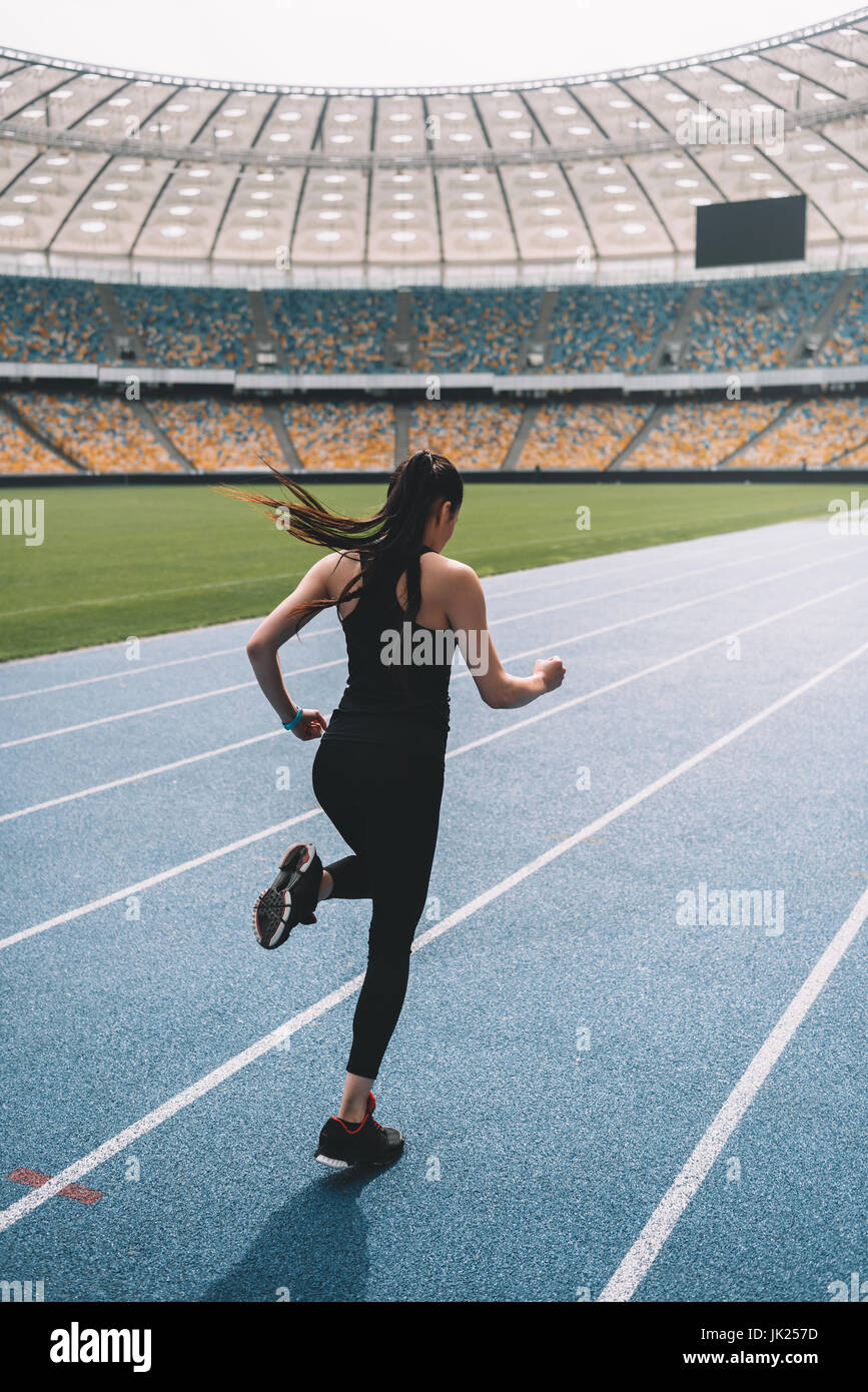 Back view of young fitness woman in sportswear sprinting on running ...