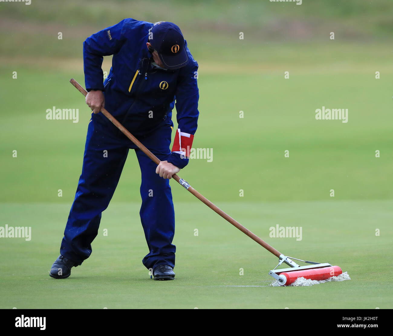 A member of ground staff sweeps the standing water on the green during ...