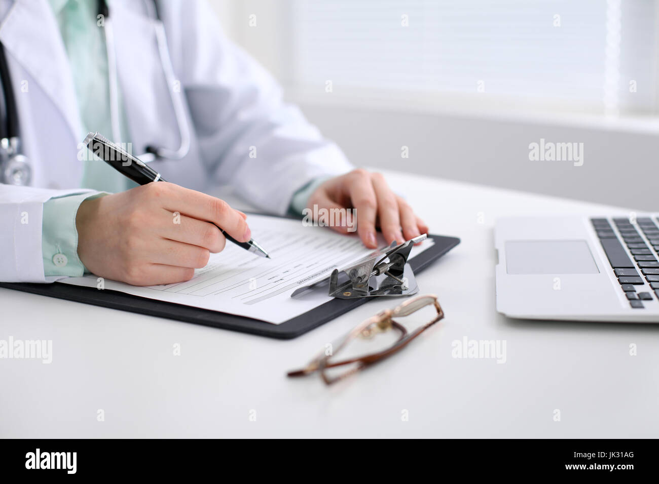 Close-up of a female doctor filling out application form , sitting at ...