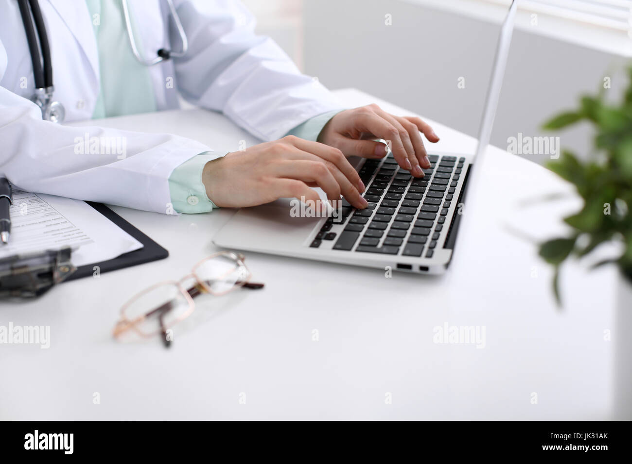 Close-up of a female doctor typing on laptop computer, sitting at the ...