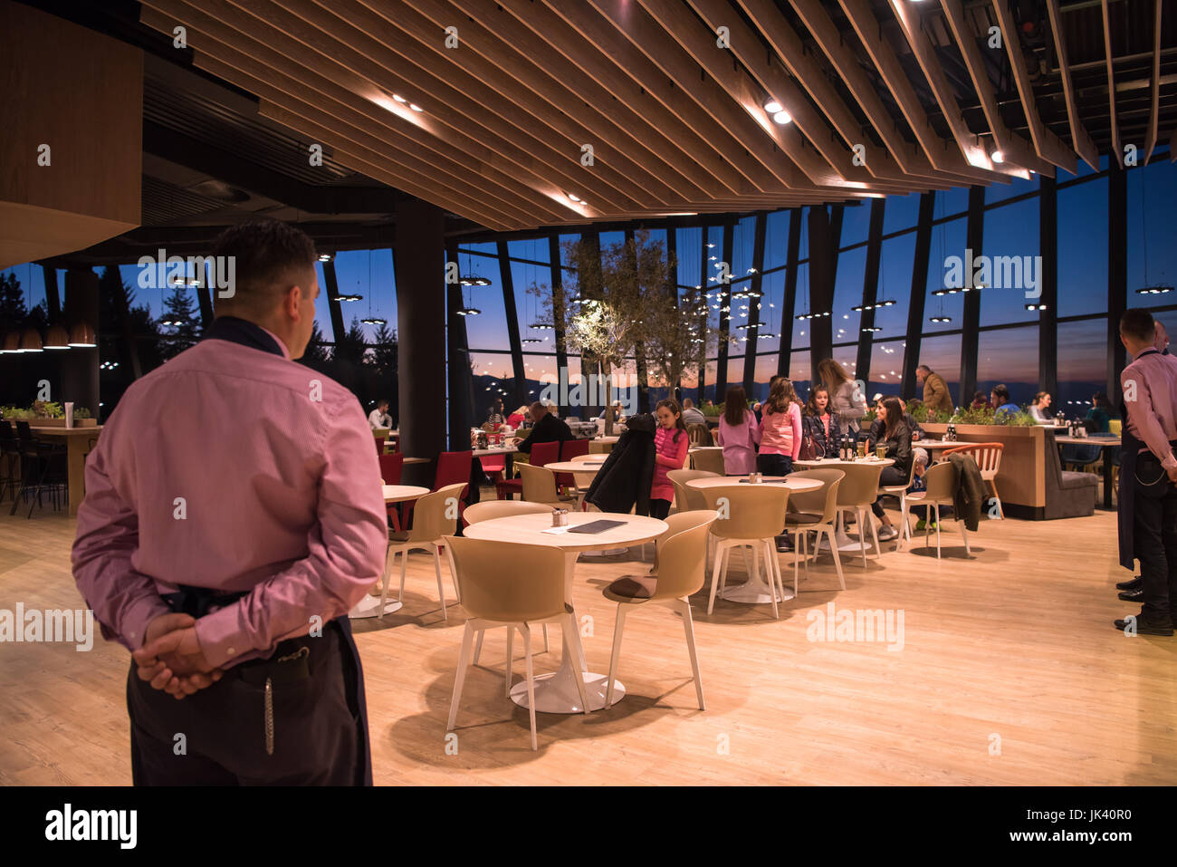 Rear view of young confident waiter standing with hands behind his back ...