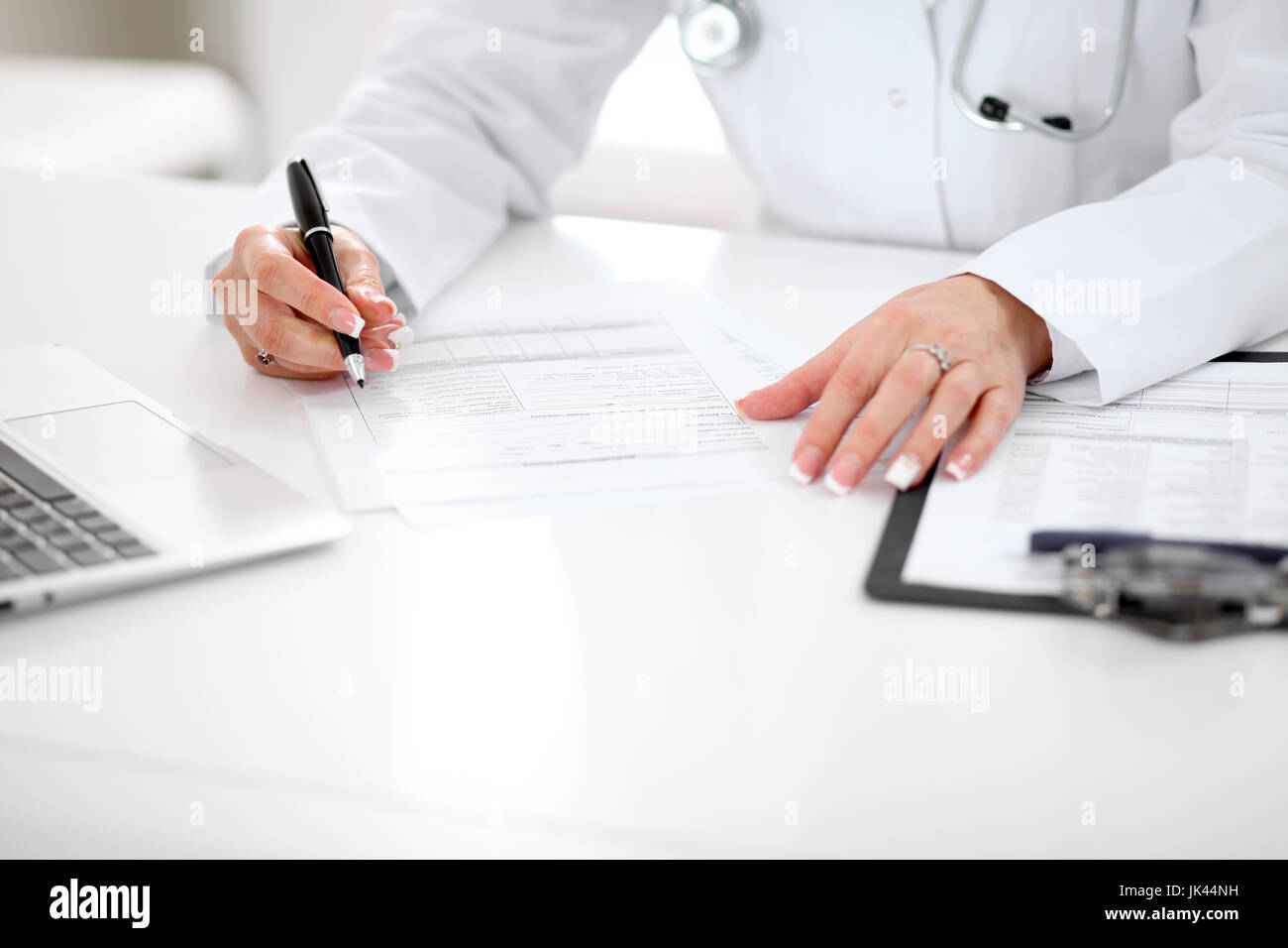 Close-up of a female doctor filling out application form , sitting at ...