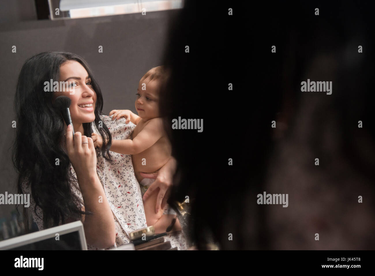 Caucasian mother holding baby son and applying makeup in mirror Stock ...