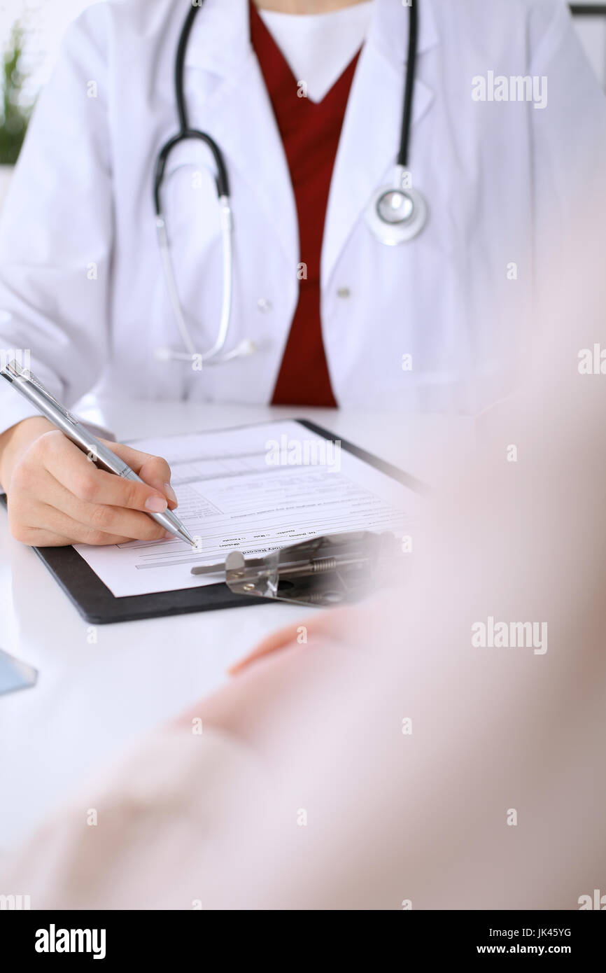 Close up of a female doctor filling up an application form while ...