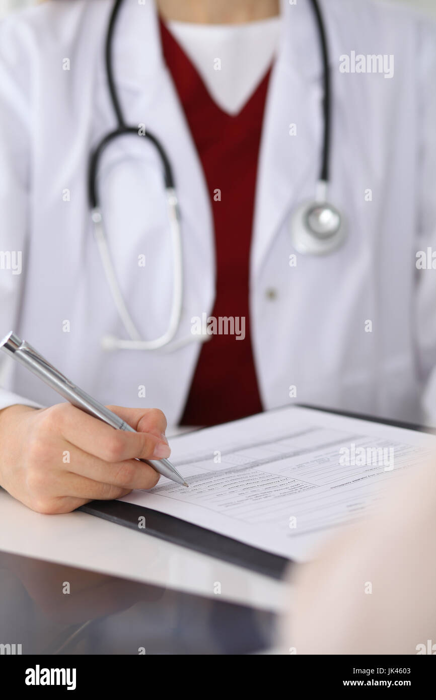 Close up of a female doctor filling up an application form while ...