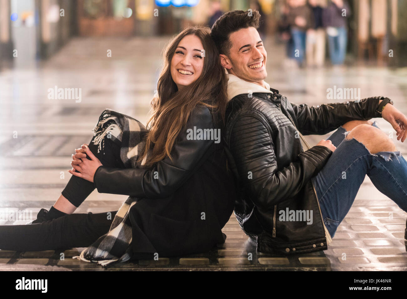 Caucasian couple sitting back to back on lobby floor Stock Photo - Alamy