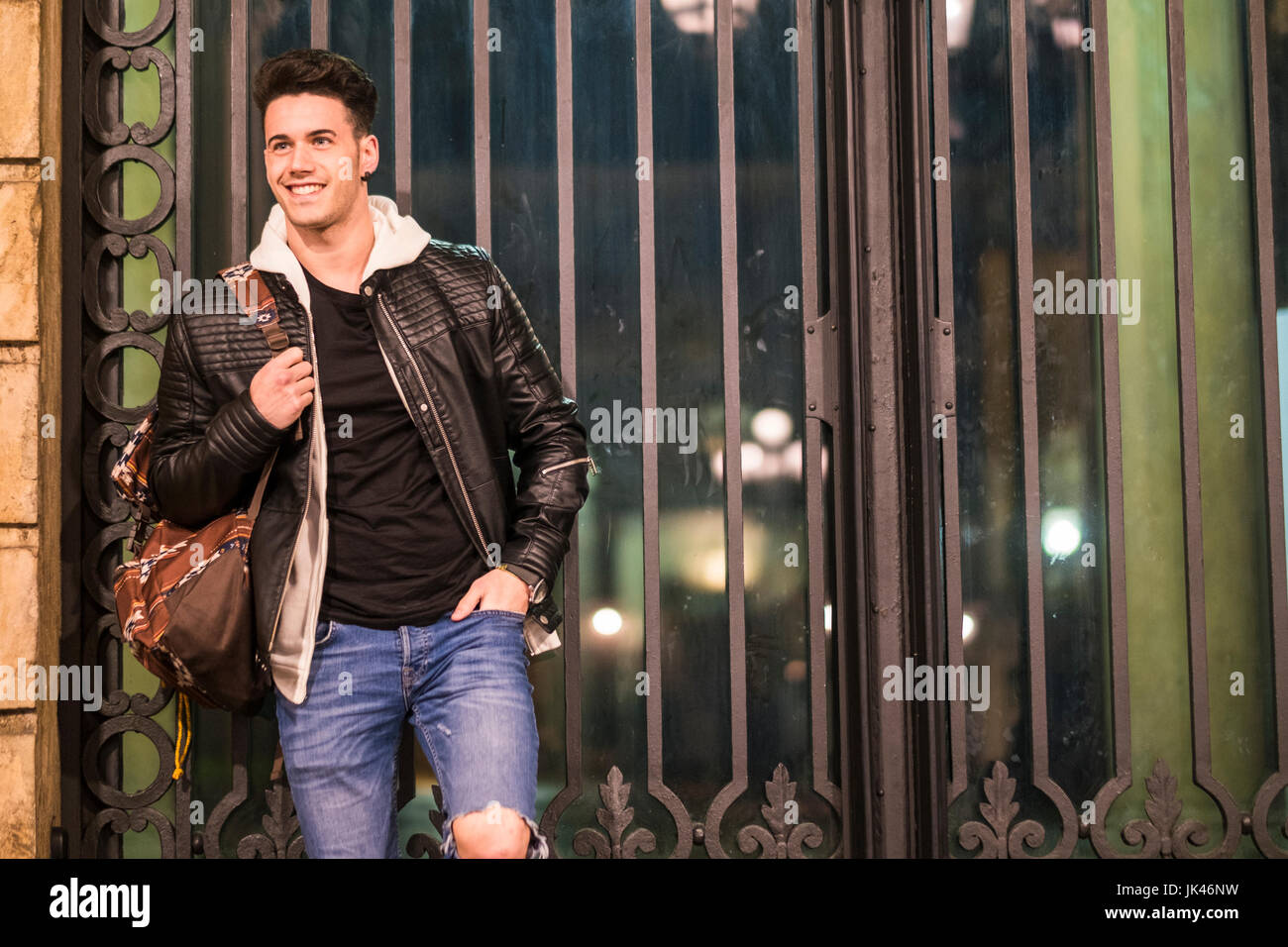 Smiling Caucasian man carrying bag leaning on gate Stock Photo - Alamy