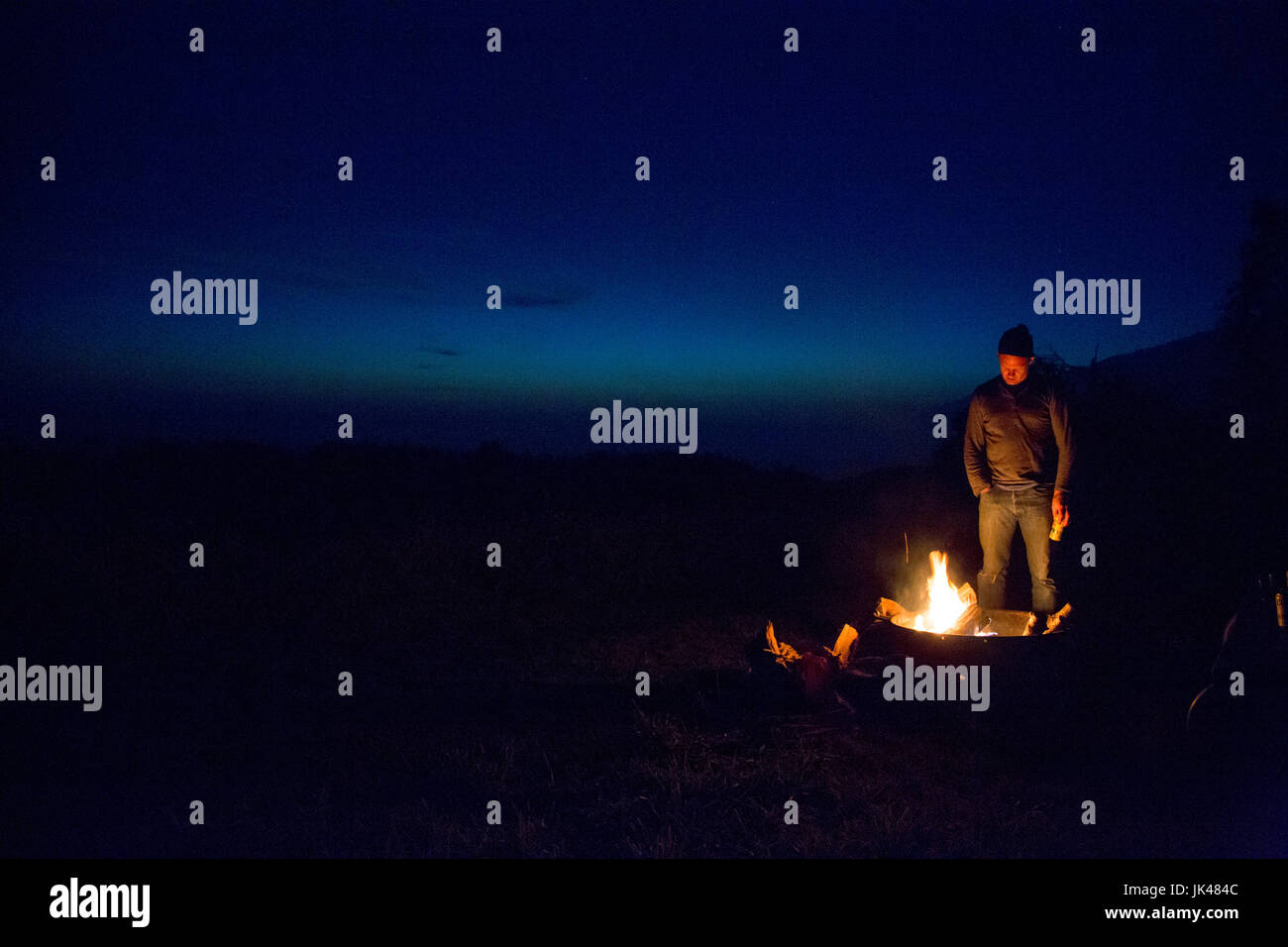 Caucasian man watching campfire at night Stock Photo - Alamy