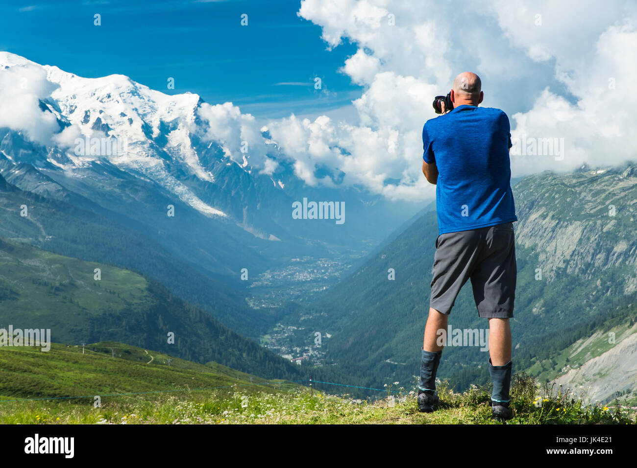 A tall bald man takes photos of the mountain valley and snow covered ...