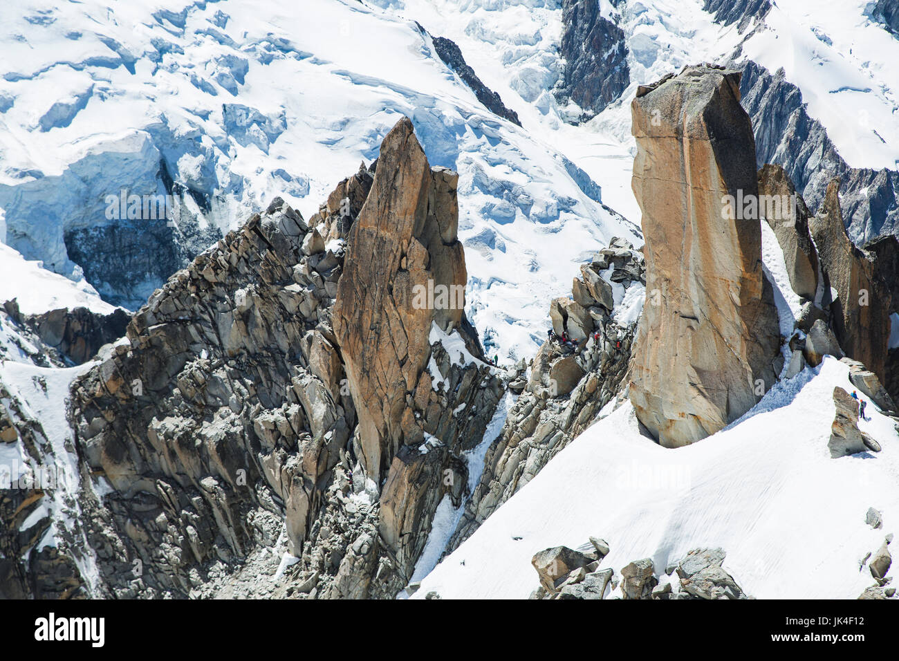 Mountaineers climb a tall stone pinnacle surrounded by ice and snow ...