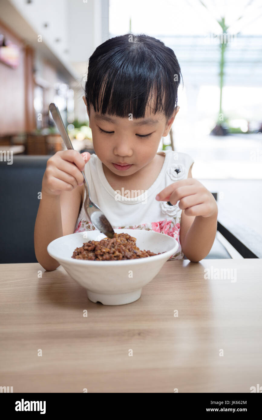 Asian little Chinese girl eating braised pork rice in outdoor cafe ...