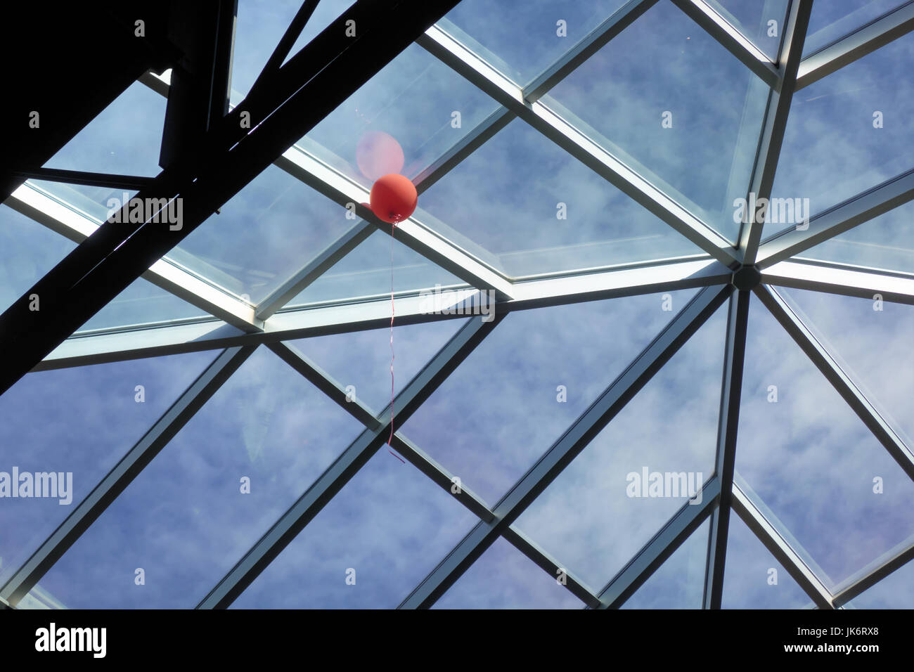 A red balloon floating up against a transparent glass and metal roof ...
