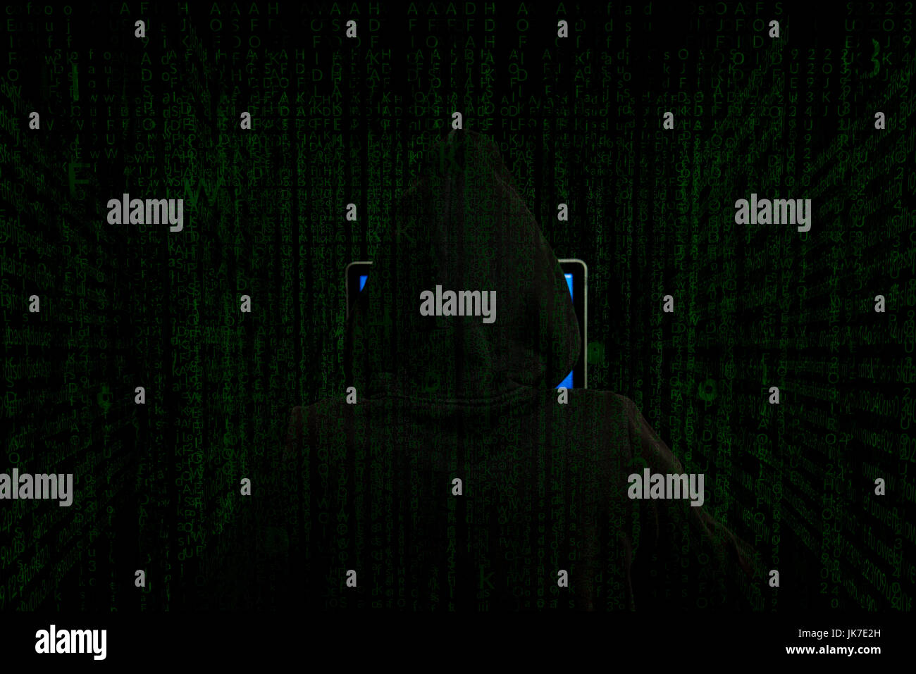 A hacker’s back view, cloaked in shadows, works at a laptop surrounded ...