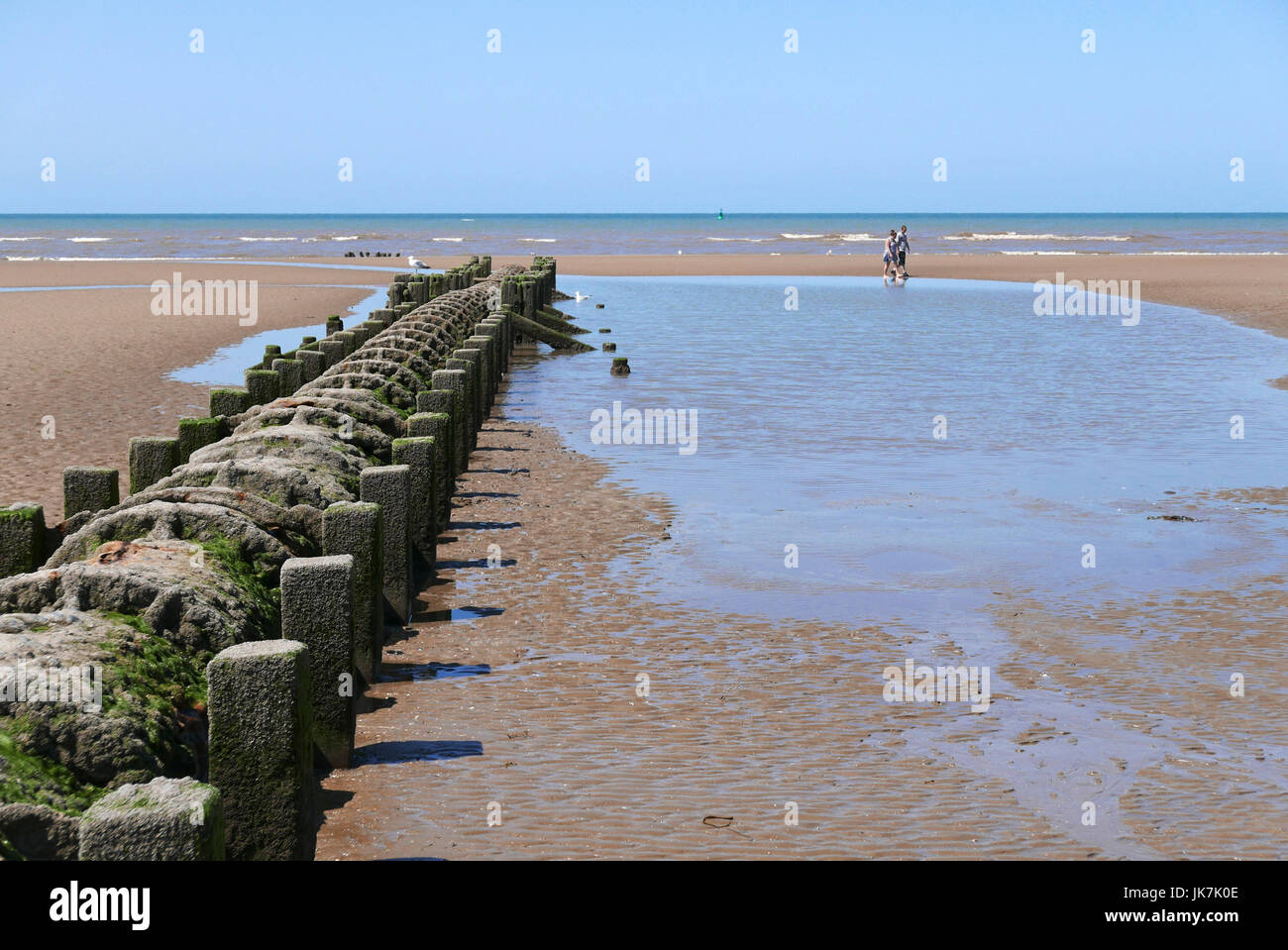 Two people walking past old barnacle covered discharge pipe on ...
